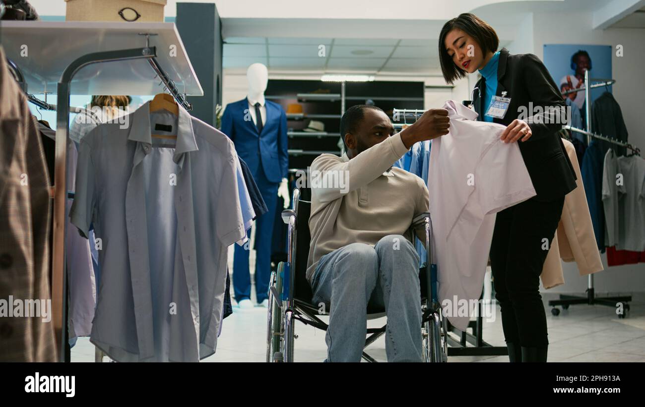 Young adult wheelchair user buying modern clothes in clothing store ...