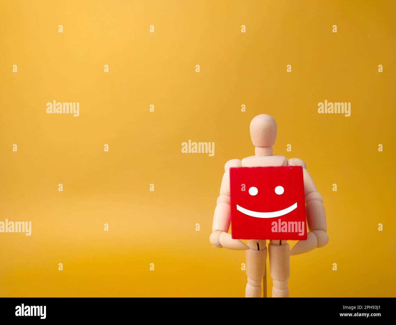 Wooden mannequin holding red cube with smile face on a yellow ...