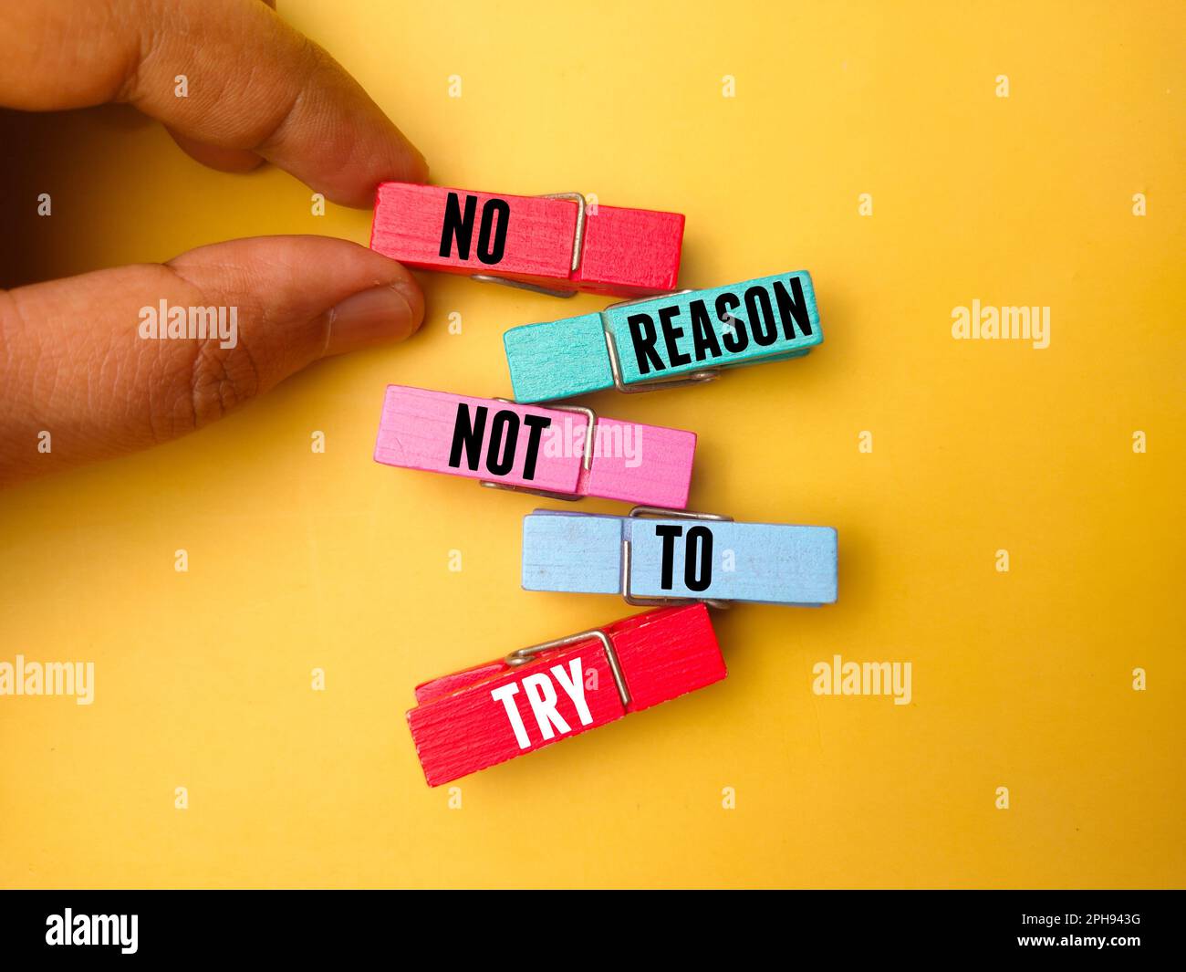 Hand holding wooden clips with the word NO REASON NOT TO TRY on yellow ... Hand holding wooden clips with the word NO REASON NOT TO TRY on yellow ...