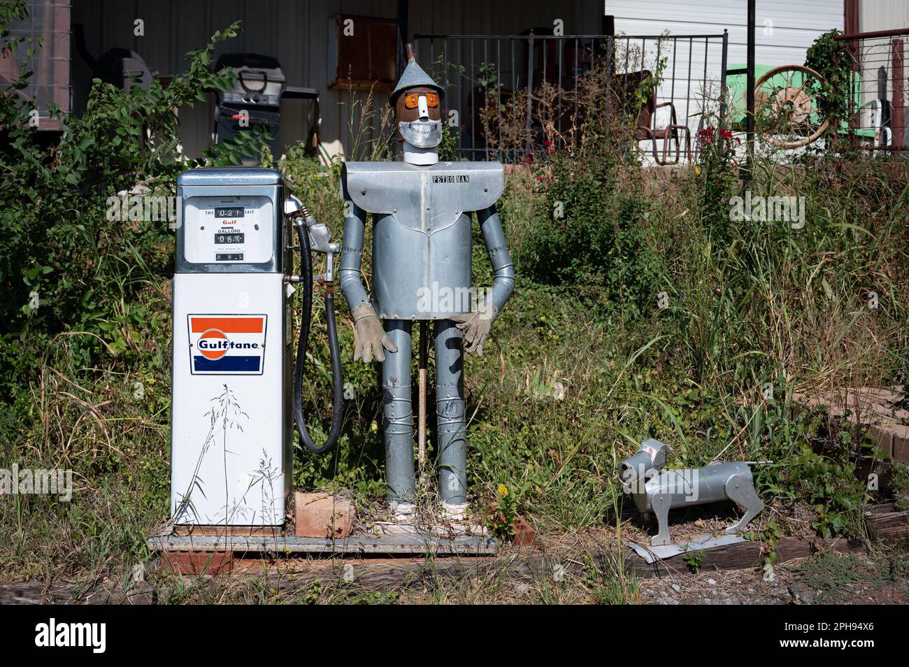 A metallic robotic figure stands next to a fuel pump in a grassy area ...