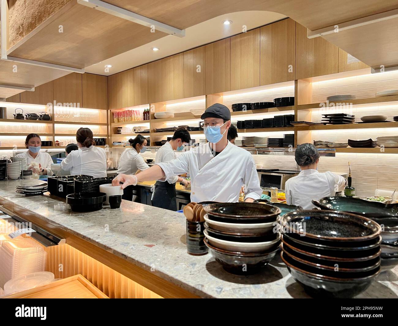 unrecognizable people in masks and gloves prepare Japanese Chinese food ...