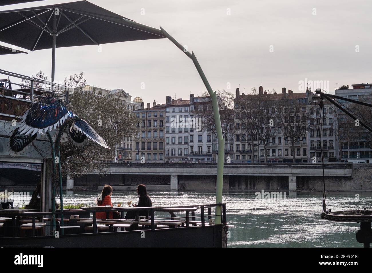 France, Lyon, 2023-03-22. Two young women having a drink on a bar barge ...