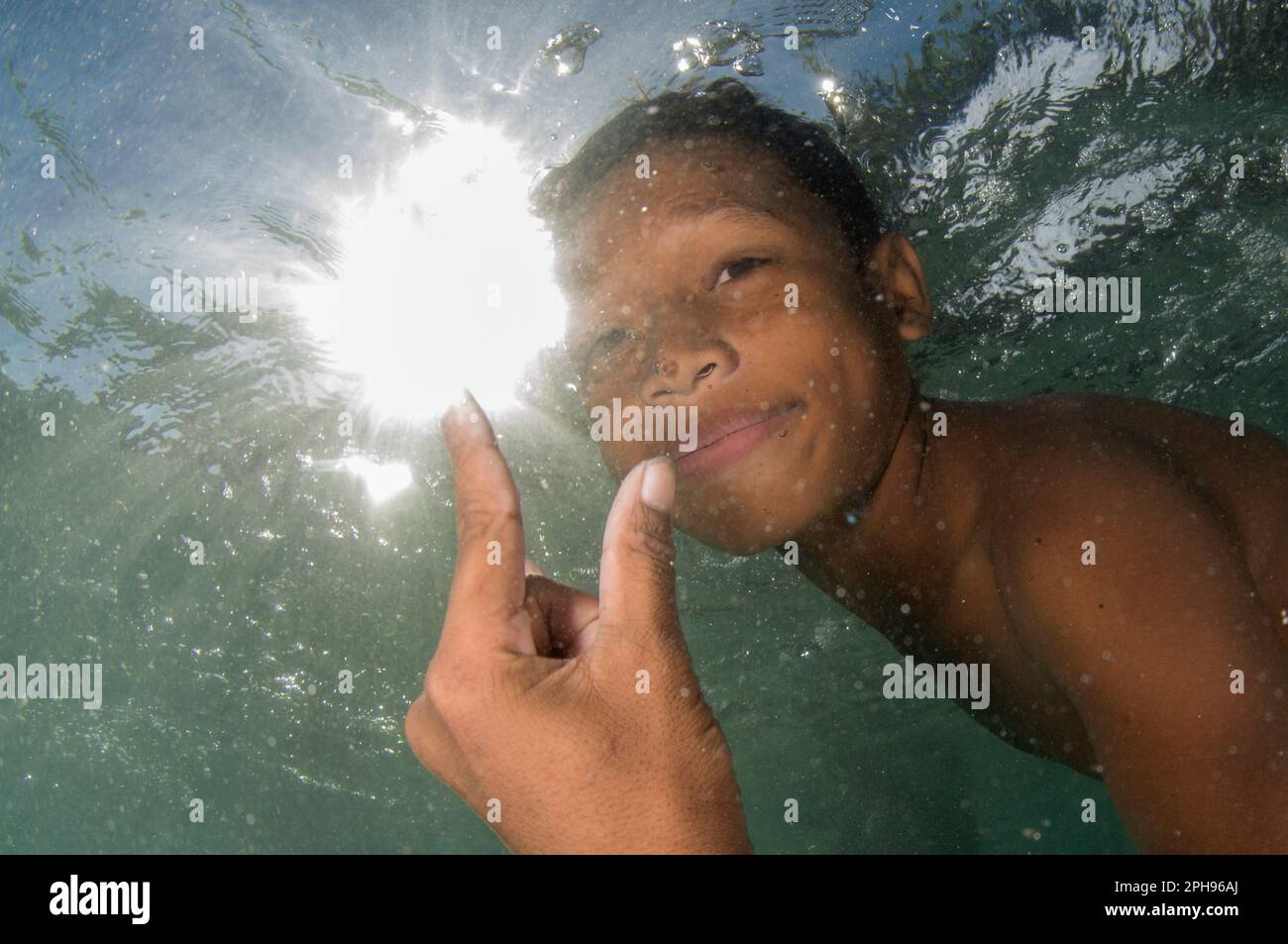 Boy playing underwater in shallow water with sun in background, Ambon ...