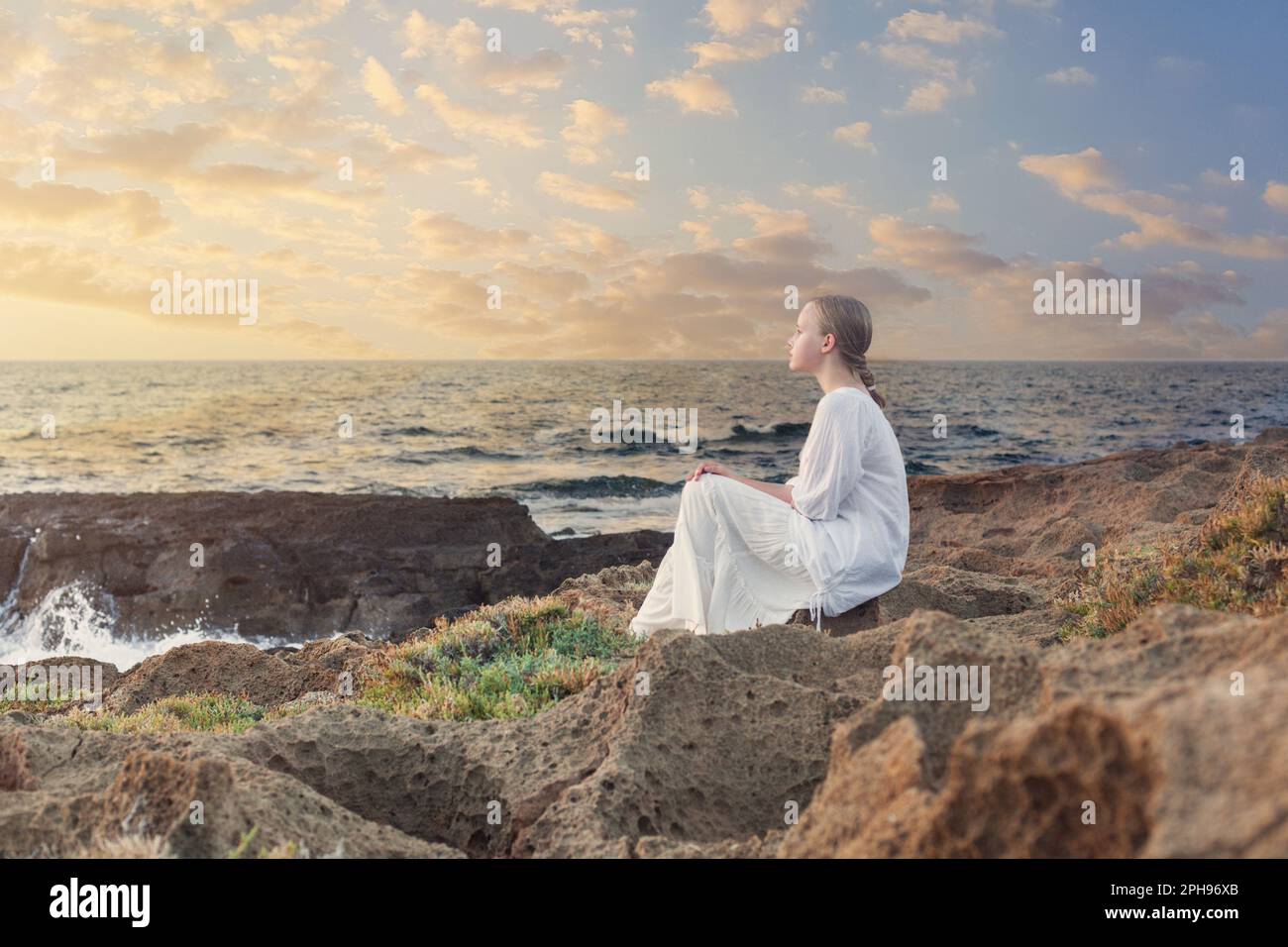 Teenage girl sitting on rocks near blue sea Stock Photo - Alamy