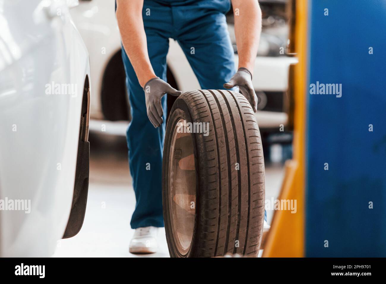 Close up view of man in work uniform with car wheel indoors. Conception ...