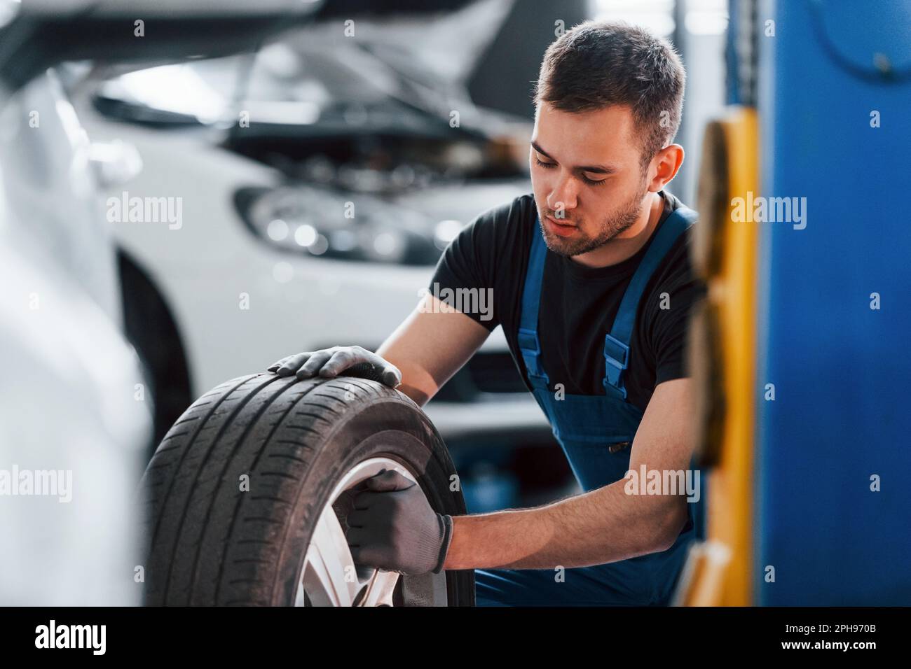 Man in work uniform sitting and changing car wheel indoors. Conception ...