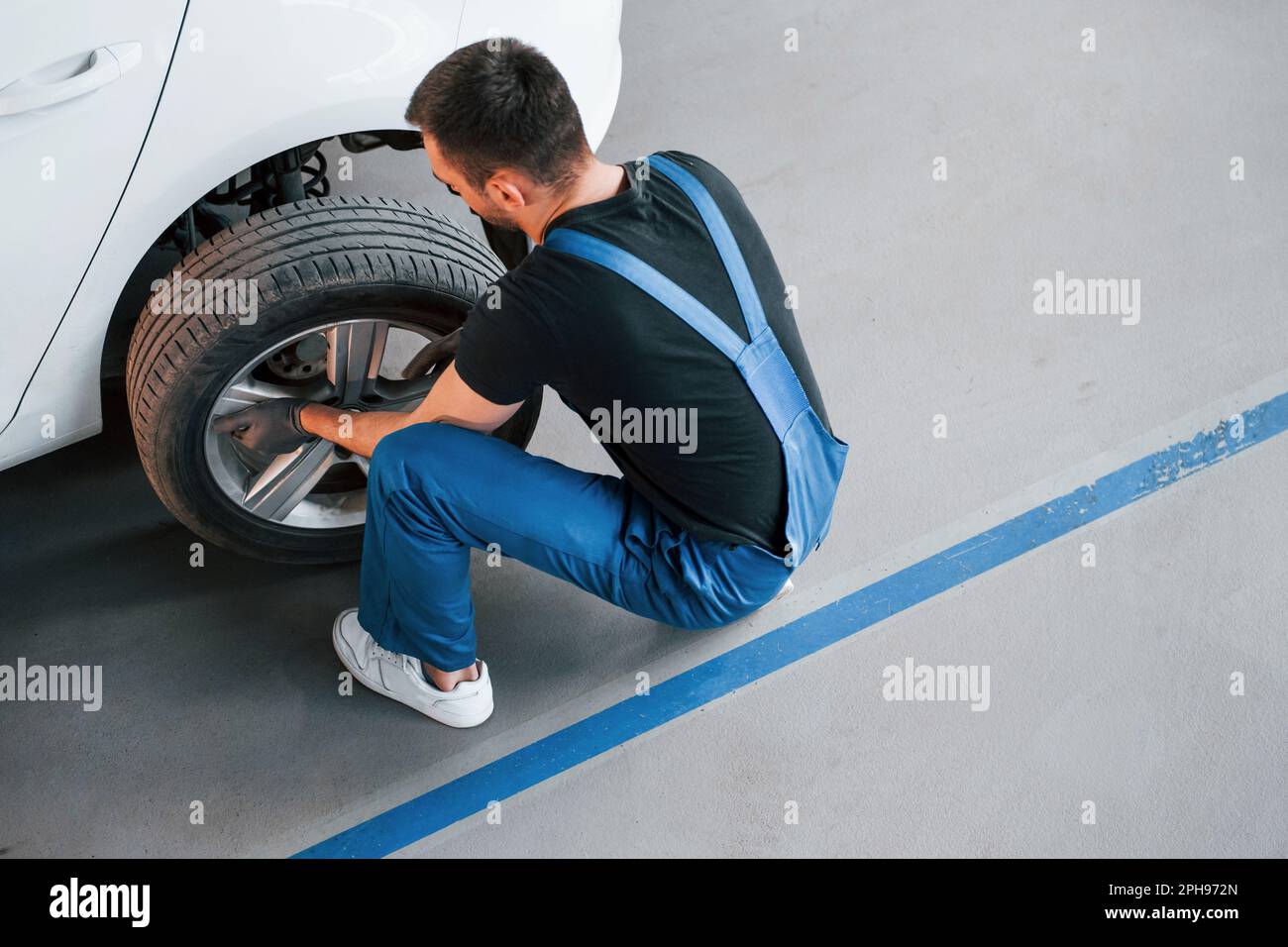 Man in work uniform sitting and changing car wheel indoors. Conception ...