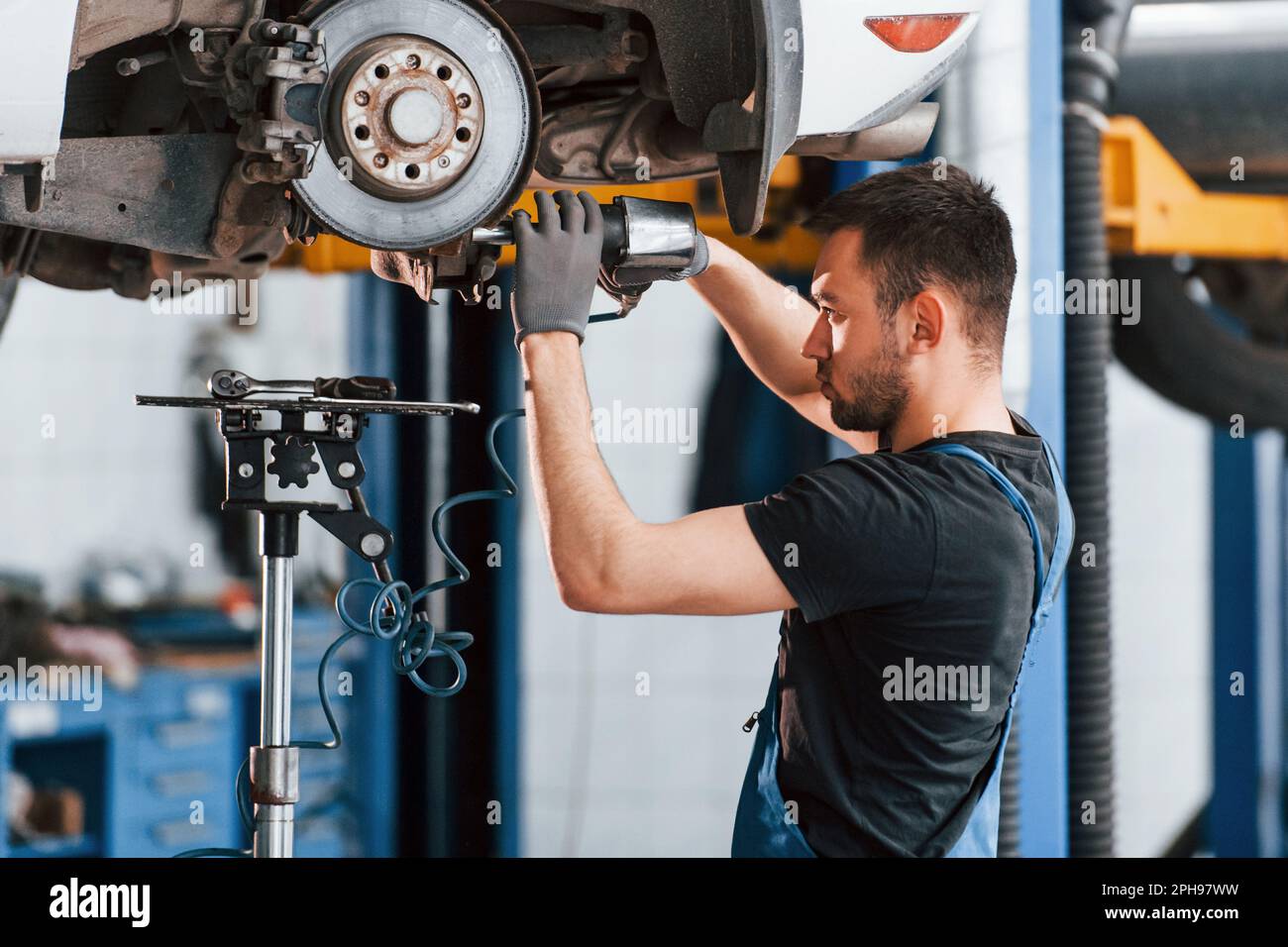 Using special tool. Man in work uniform repairs white automobile ...