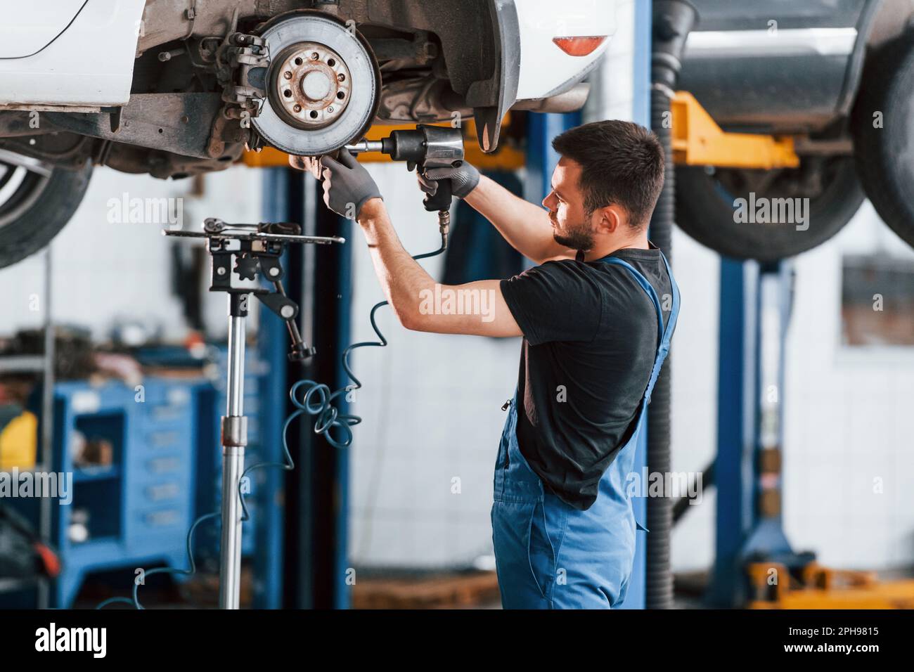 Using special tool. Man in work uniform repairs white automobile ...
