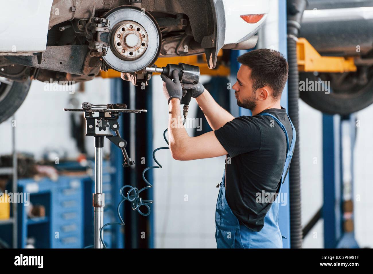 Using special tool. Man in work uniform repairs white automobile ...