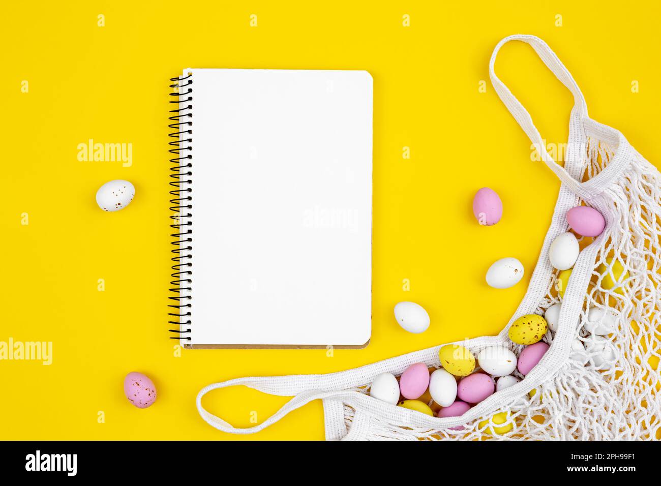 Colored Easter eggs in a mesh bag and a blank notepad on a yellow ...