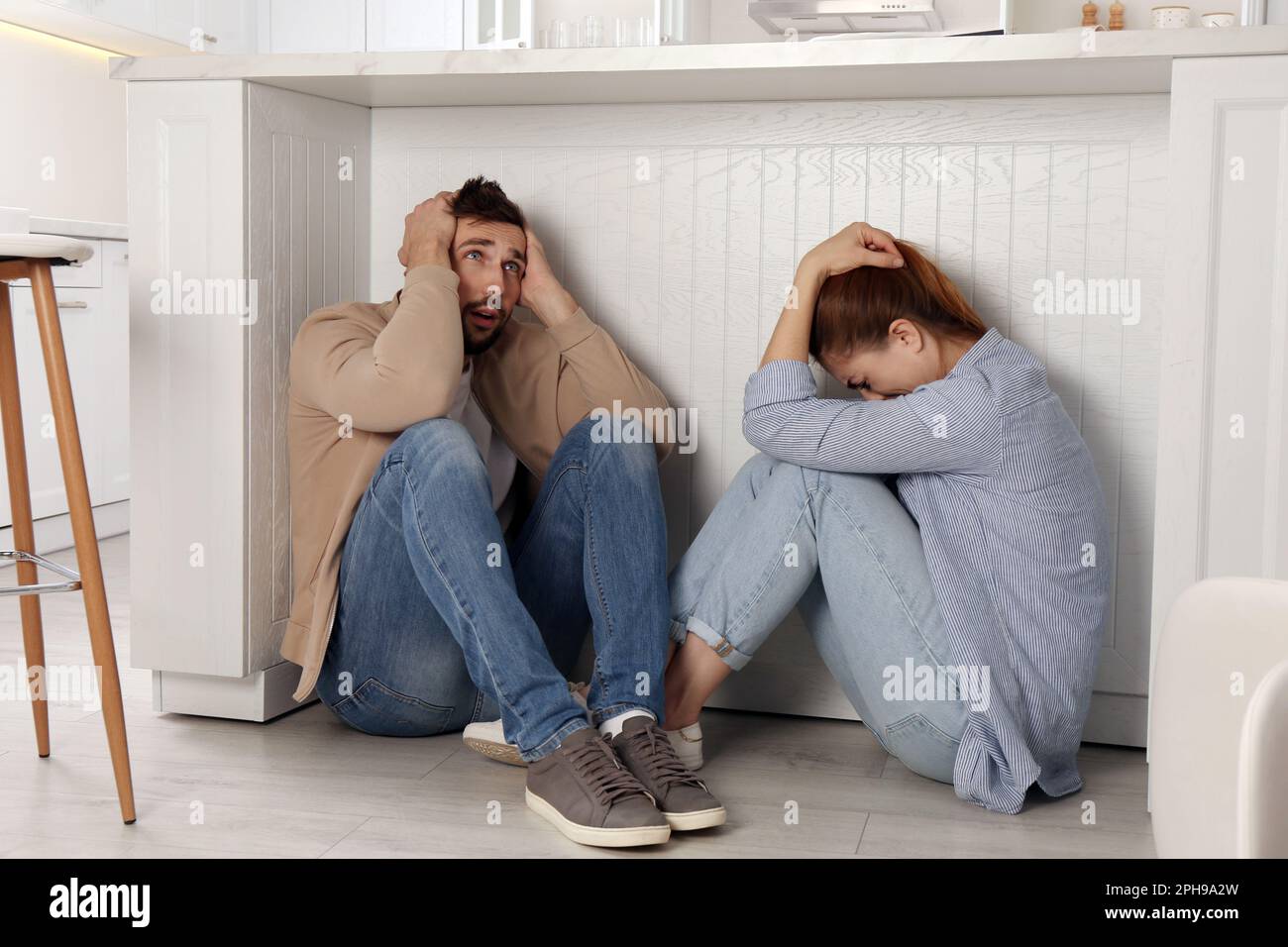 Scared couple hiding under table in kitchen during earthquake Stock ...