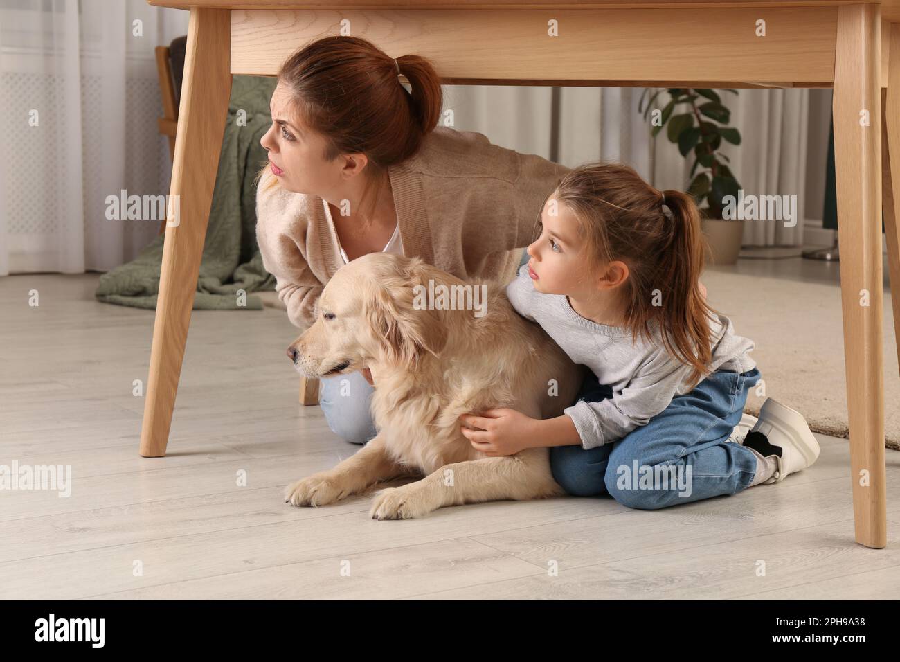 Scared mother with her little daughter and dog hiding under table in ...
