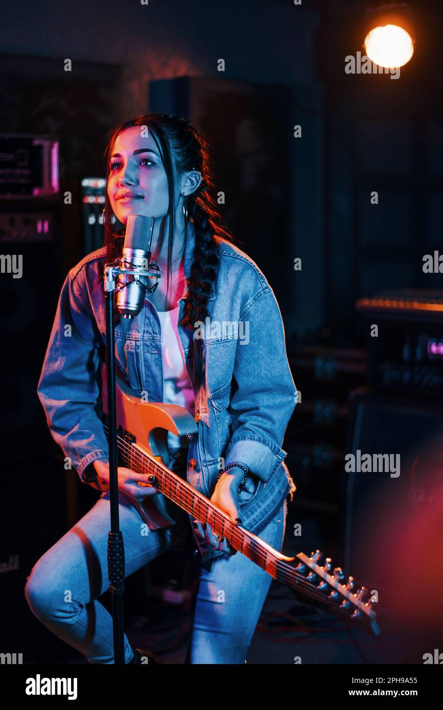 Young beautiful female performer with guitar singing and rehearsing in ...