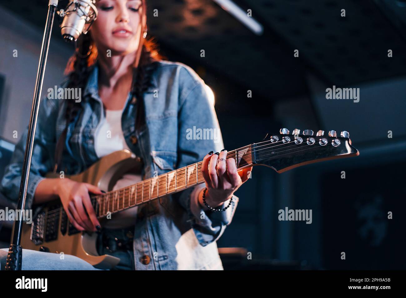 Young beautiful female performer with guitar singing and rehearsing in ...