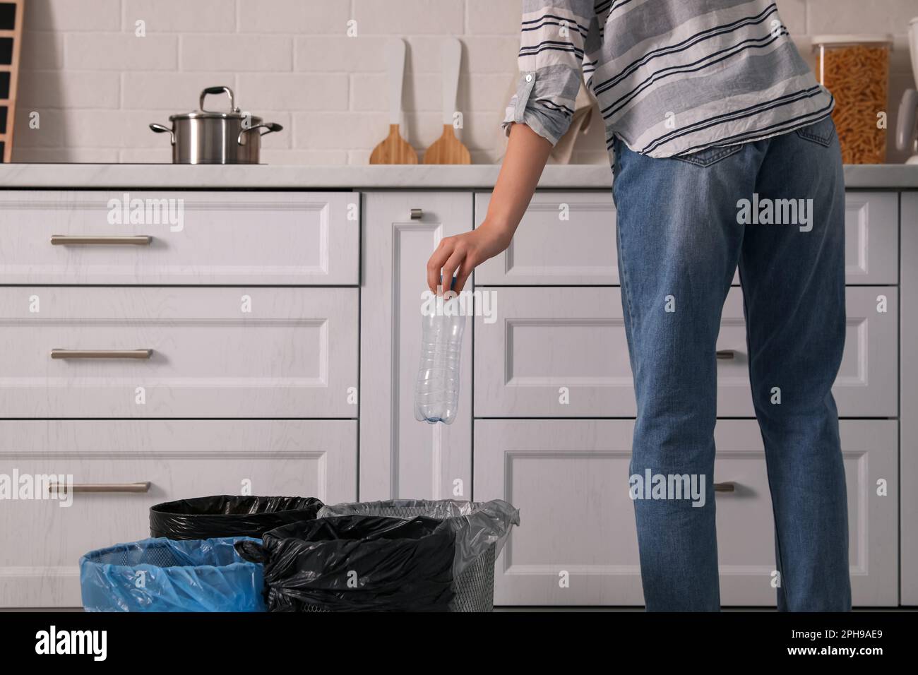 Woman throwing plastic bottle into trash bin in kitchen, closeup ...