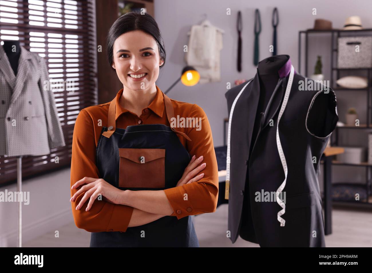 Happy dressmaker near mannequin with unfinished garment and measuring ...