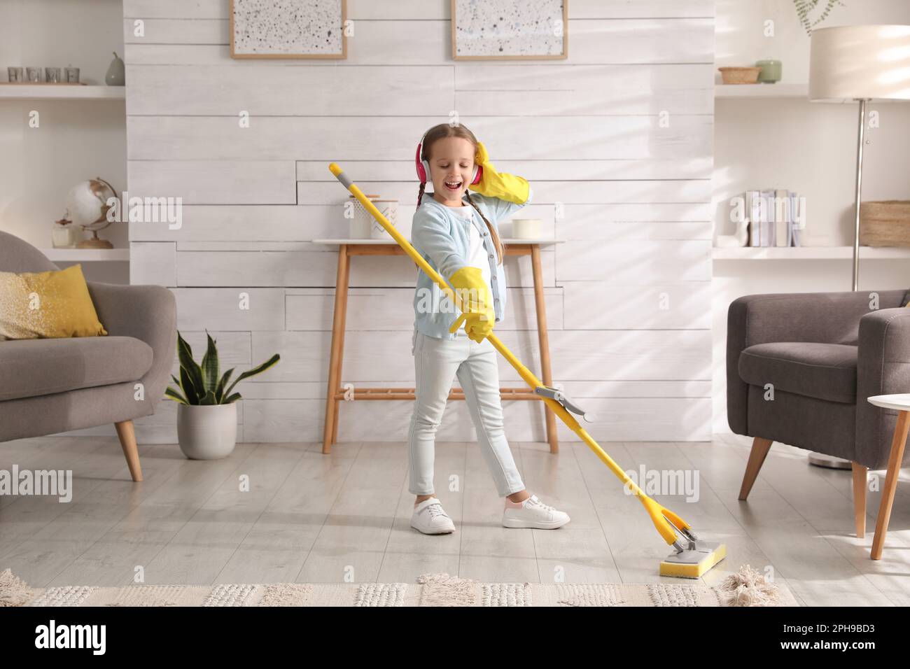 Cute little girl in headphones with mop singing while cleaning at home ...
