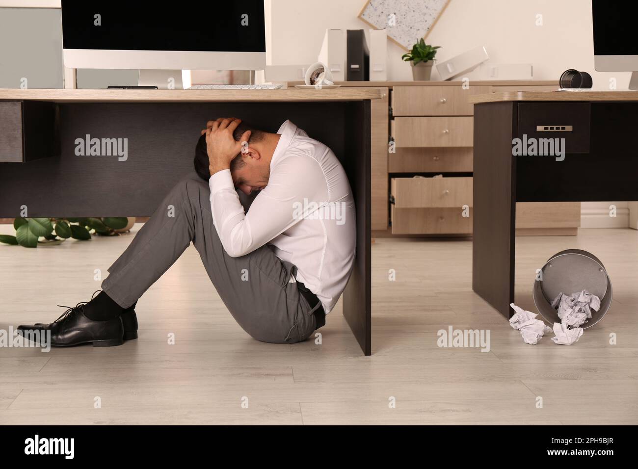 Scared man hiding under office desk during earthquake Stock Photo - Alamy