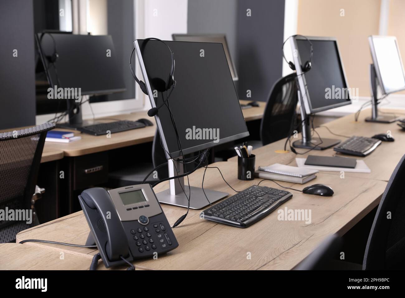 Modern computers with headsets and stationary phone on wooden desk in ...