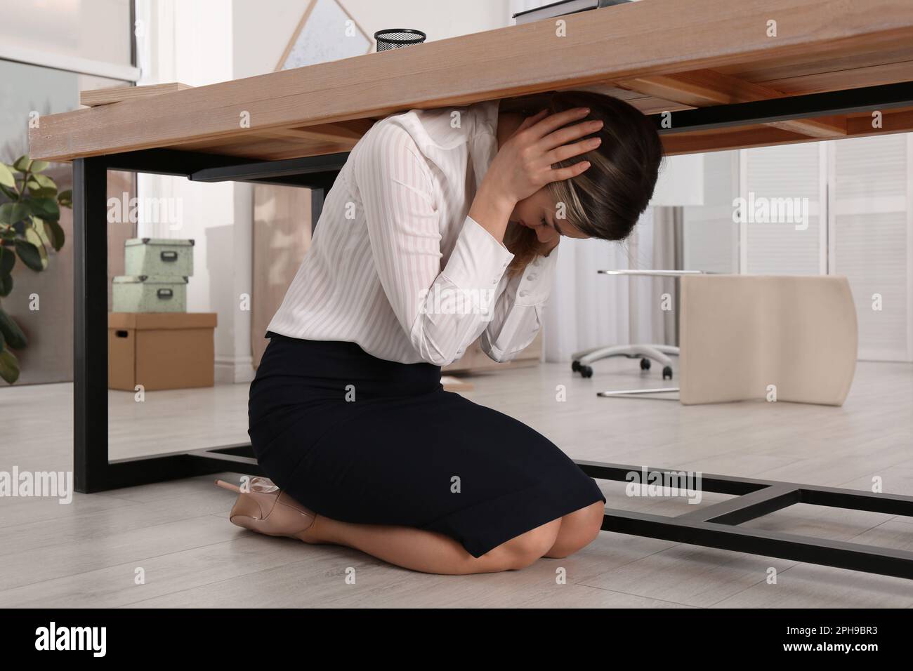 Scared young woman hiding under office desk during earthquake Stock ...