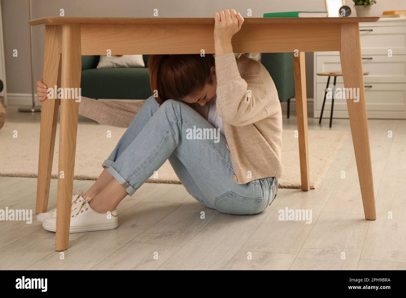 Scared woman hiding under table in living room during earthquake Stock ...
