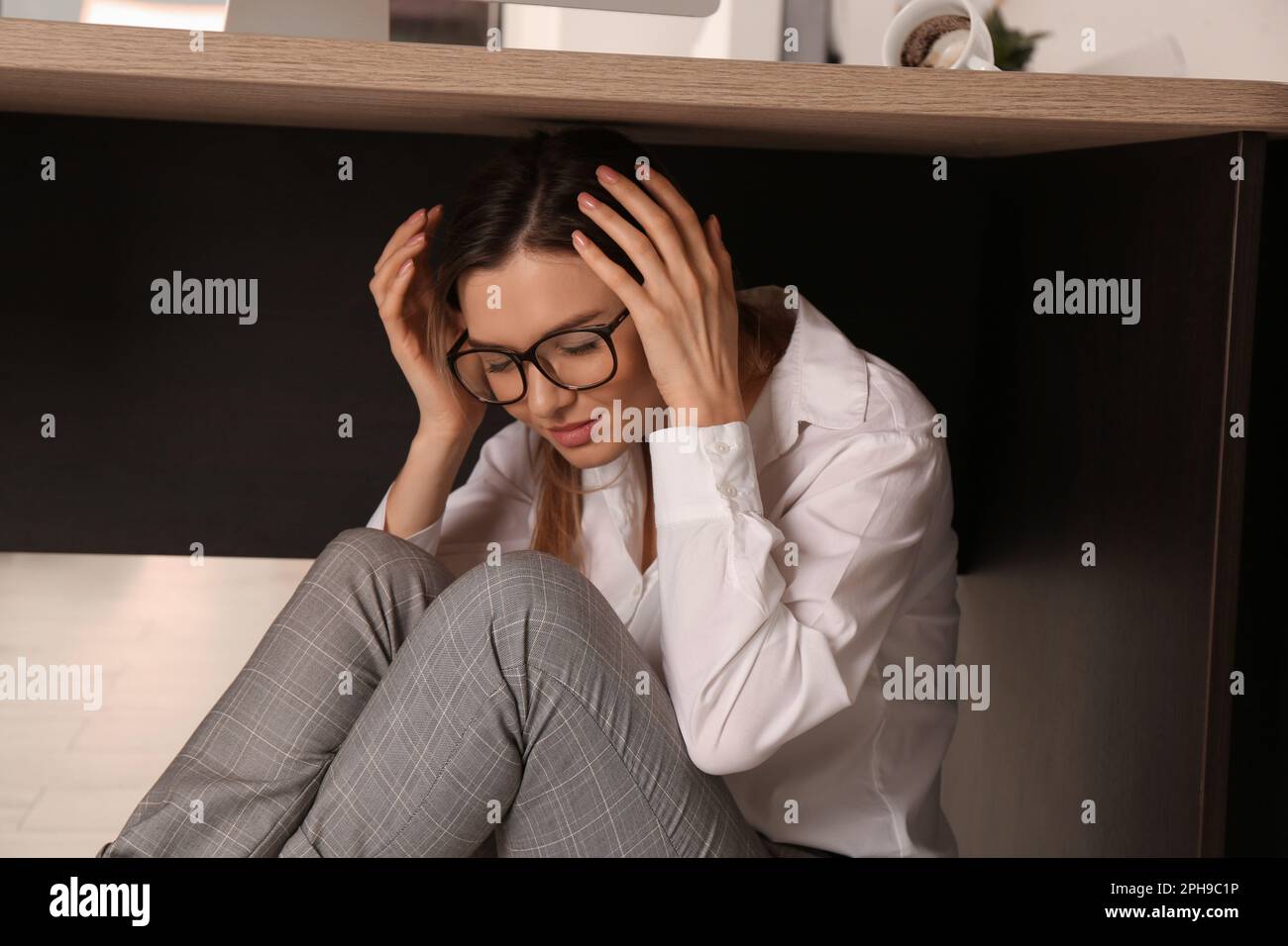 Scared young woman hiding under office desk during earthquake Stock ...