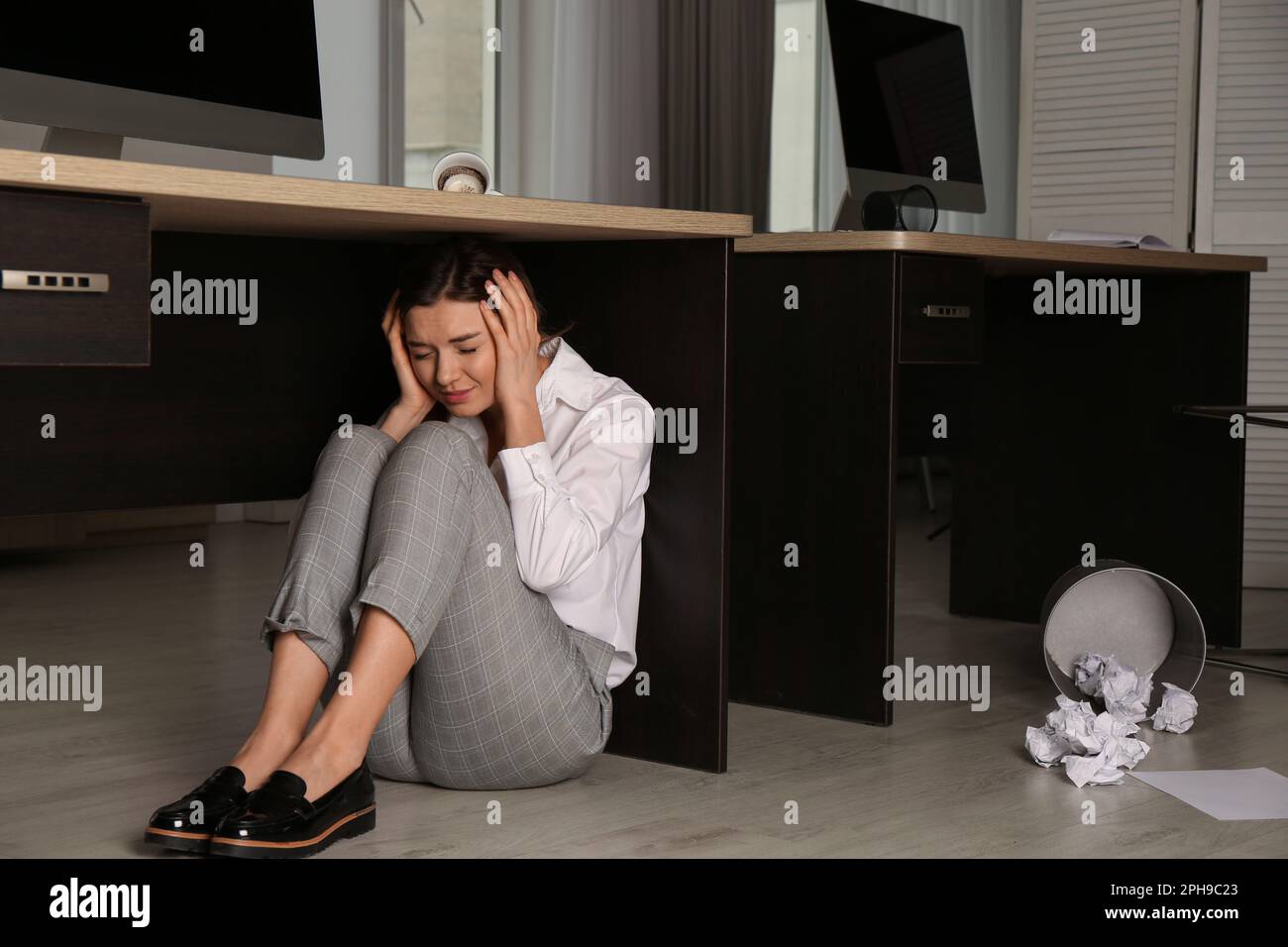 Scared young woman hiding under office desk during earthquake Stock ...