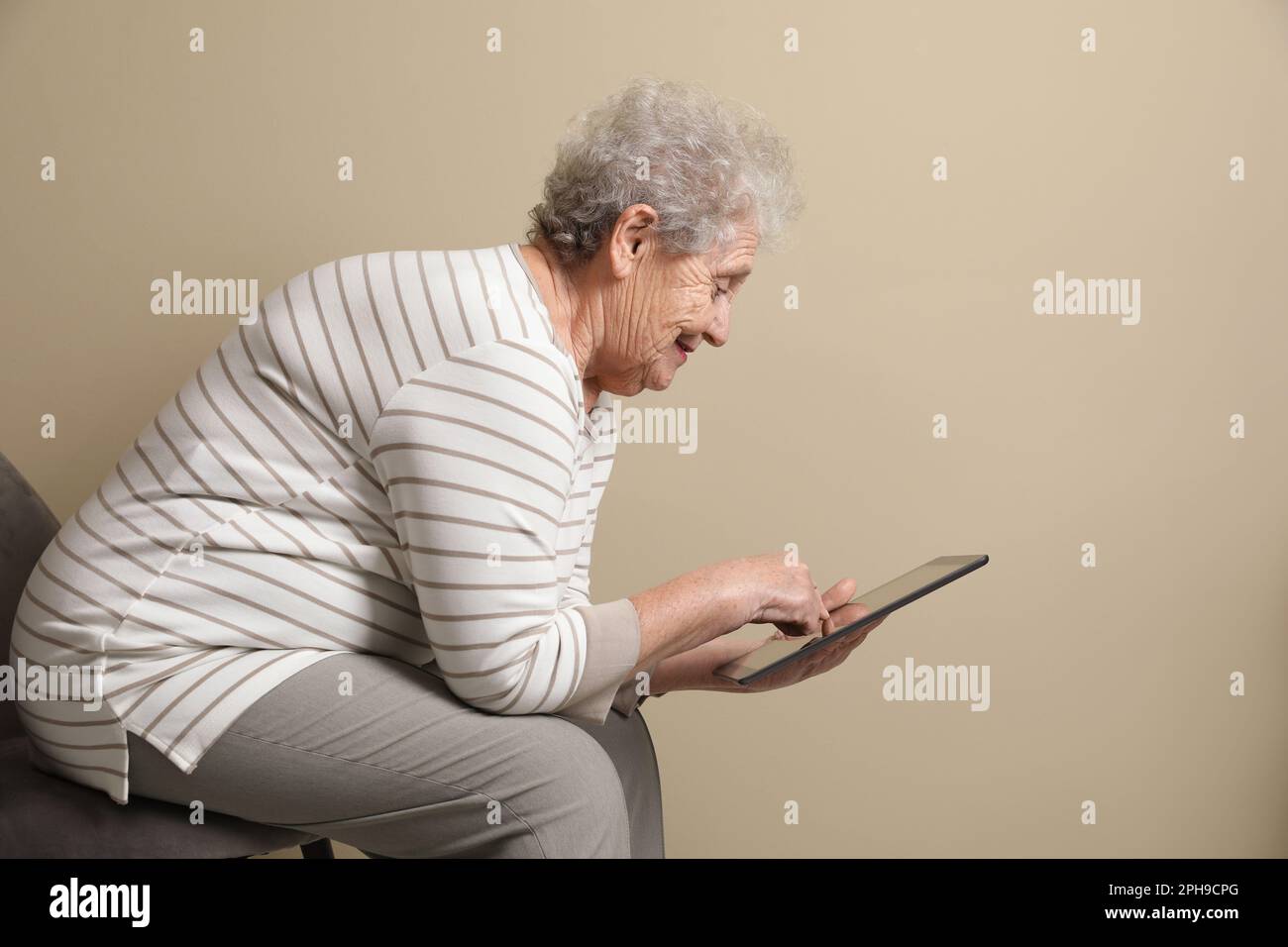 Elderly woman with poor posture using tablet on beige background Stock ...