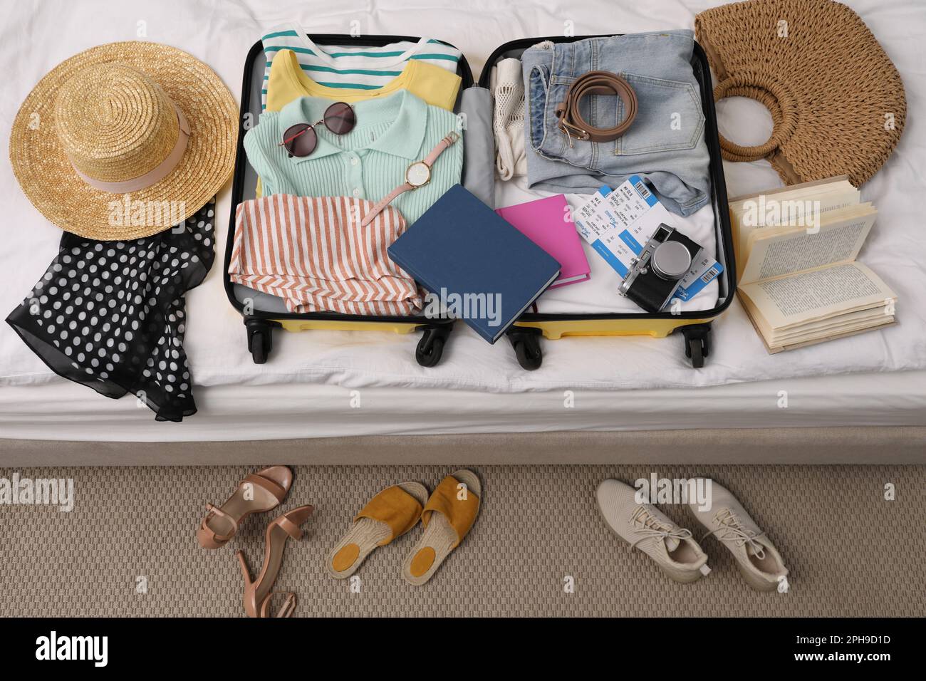 Open suitcase with clothes and accessories on bed indoors, top view ...