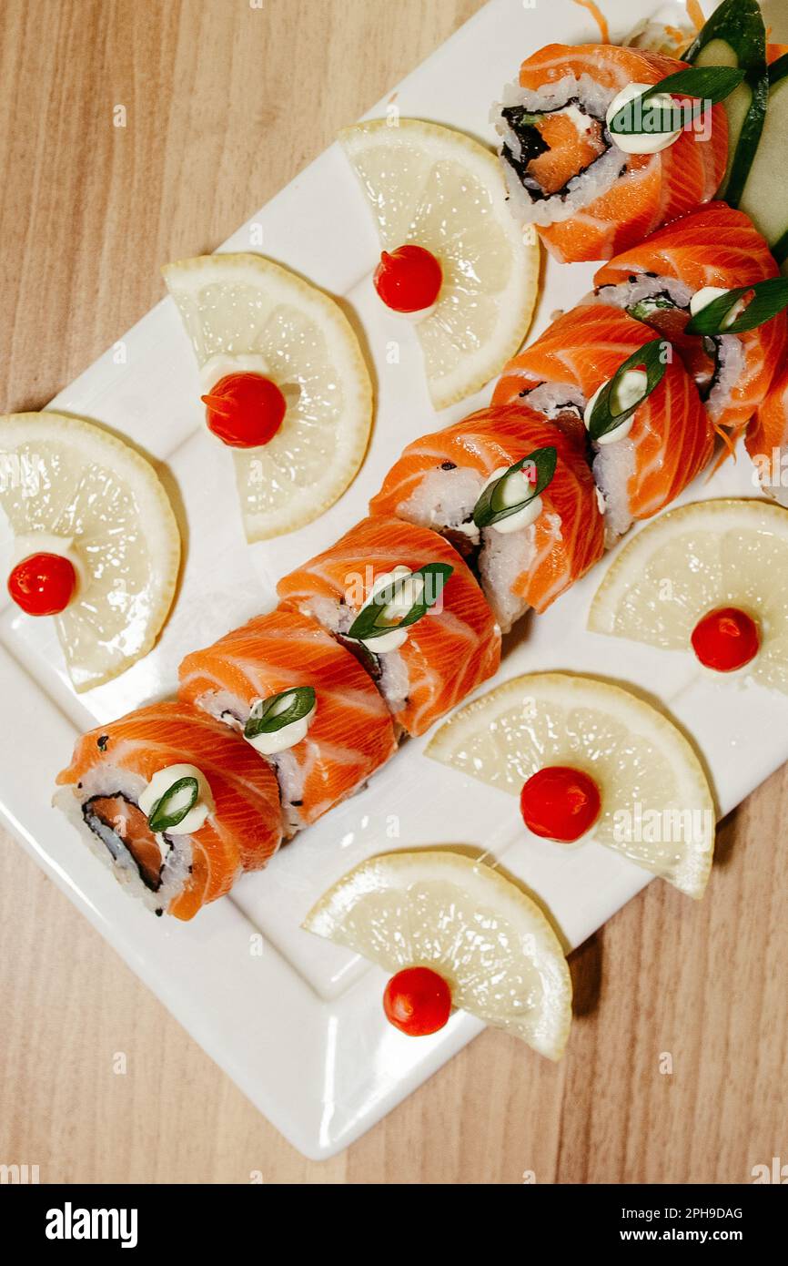 A variety of sushi rolls arranged on a rectangular platter, presented ...