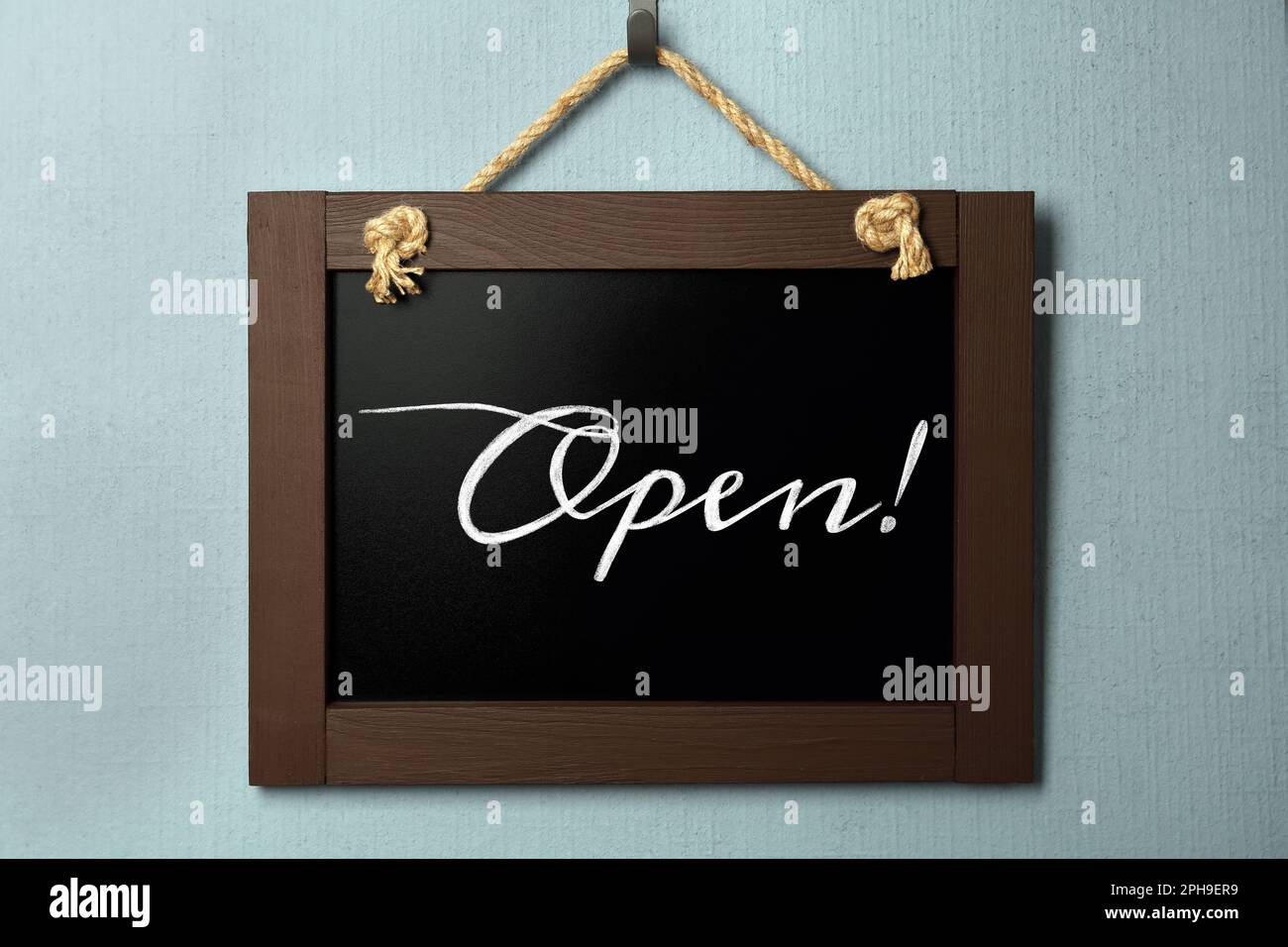 Small chalk board with word Open on light blue wall Stock Photo - Alamy