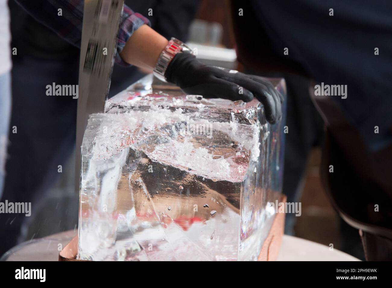A professional bartender cutting ice from a large block to prepare ...