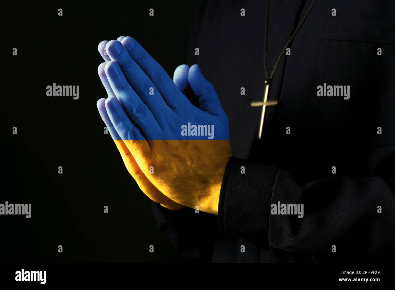 Pray for Ukraine. Priest on dark background, closeup. Hands toned in ...