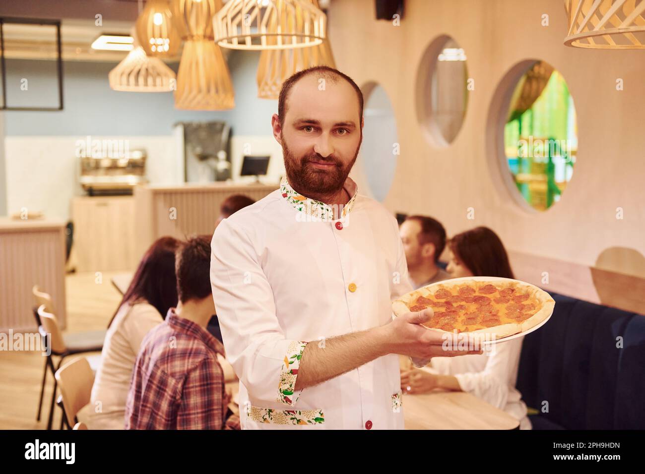 Chef standing with pizza in hands against group of young friends that ...