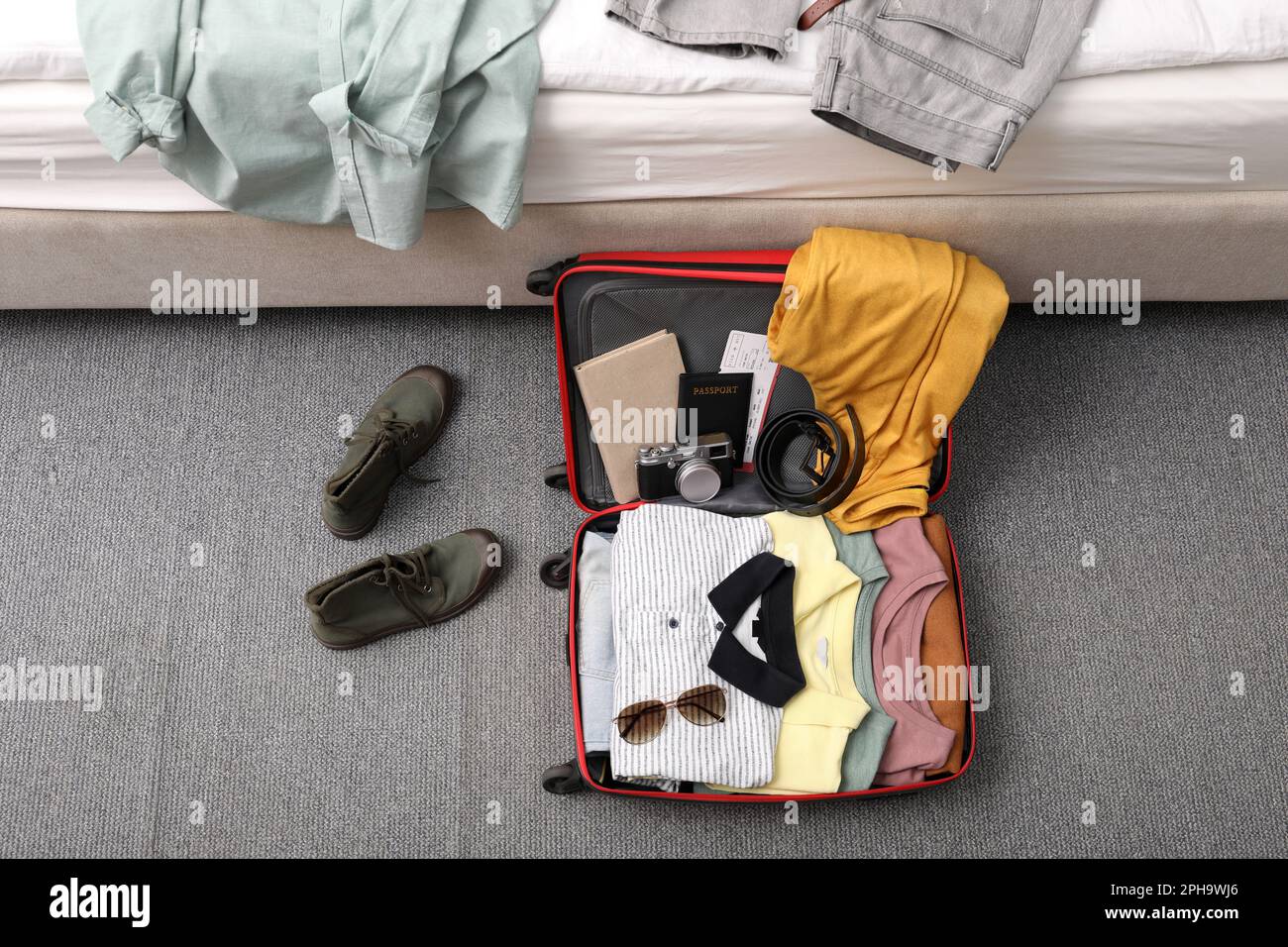 Open suitcase with clothes, accessories and shoes on floor near bed ...