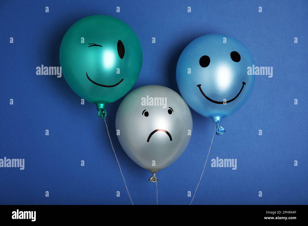 Balloon with sad face among happy ones on blue background. Depression ...