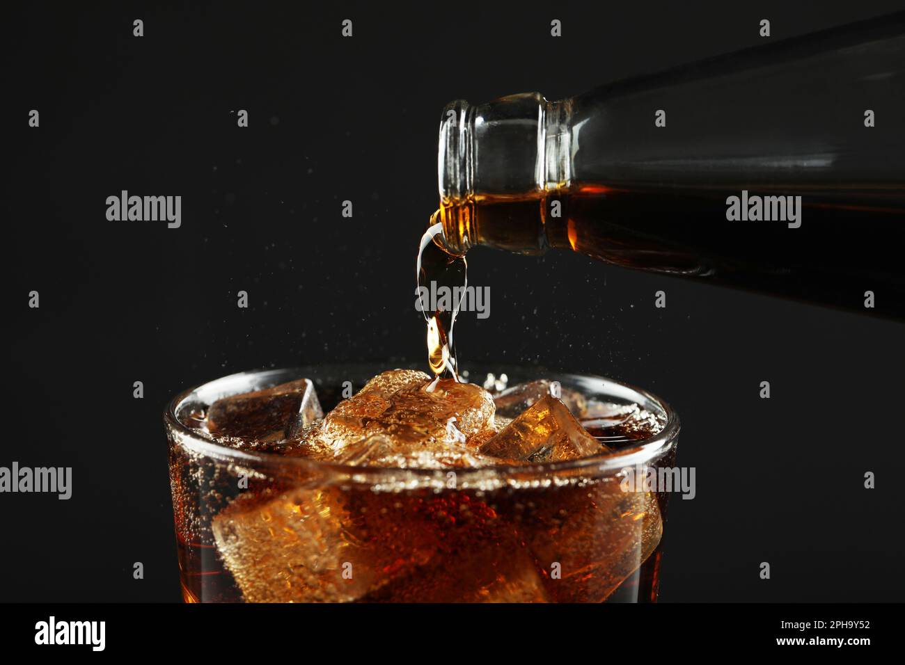 Pouring refreshing soda water from bottle into glass on black ...