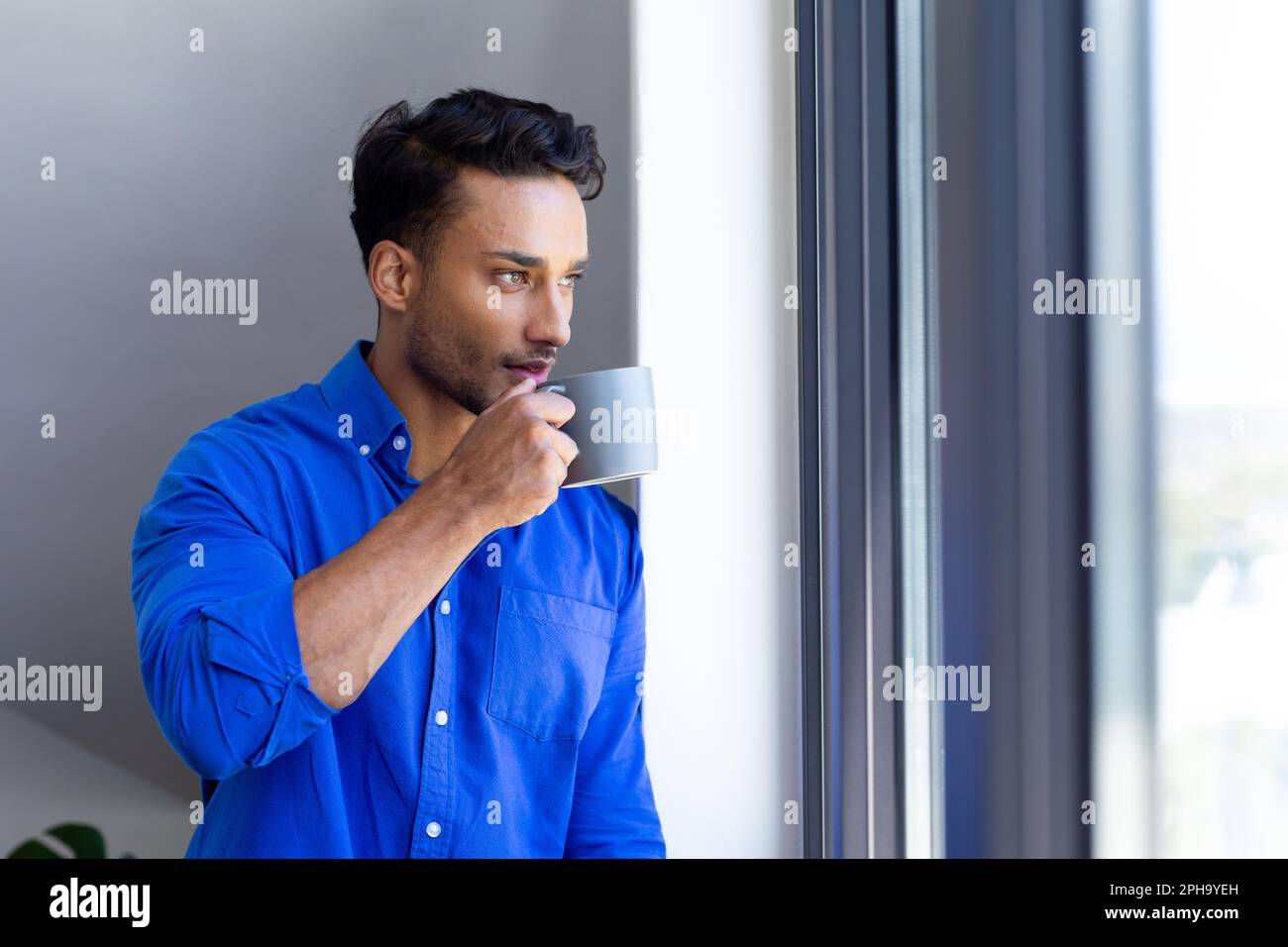 Happy biracial man drinking coffee and looking through window Stock ...
