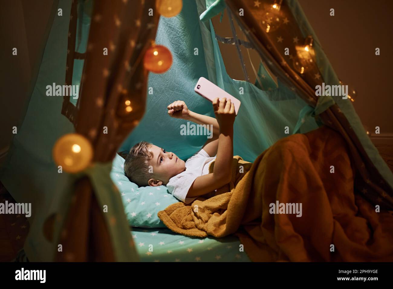 Using phone. Young boy in casual clothes lying down in tent at evening ...