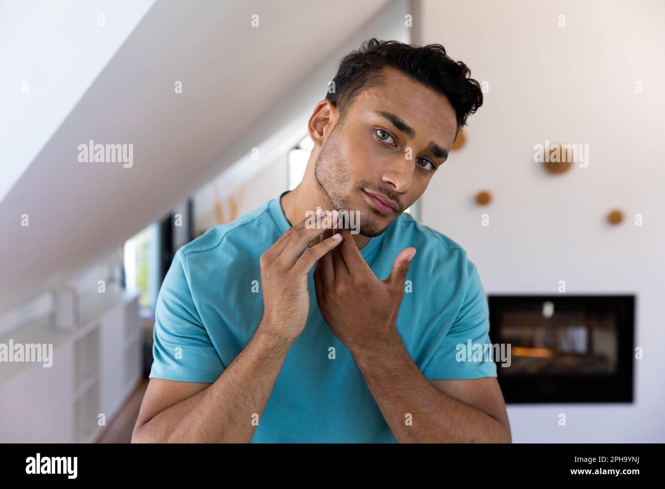 Biracial man touching his face, looking at himself in bathroom mirror ...