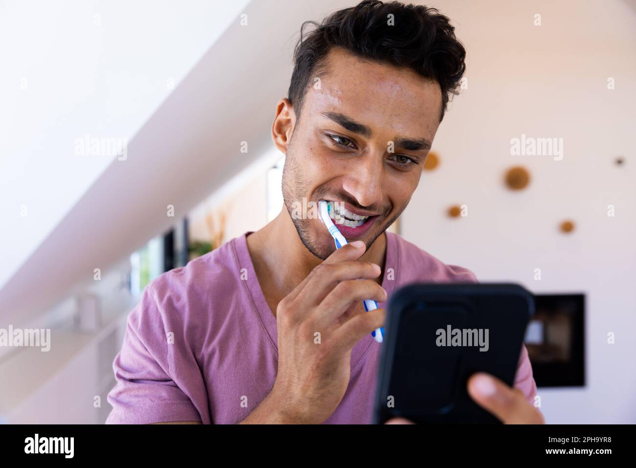 Happy biracial man brushing teeth and using smartphone in bathroom ...