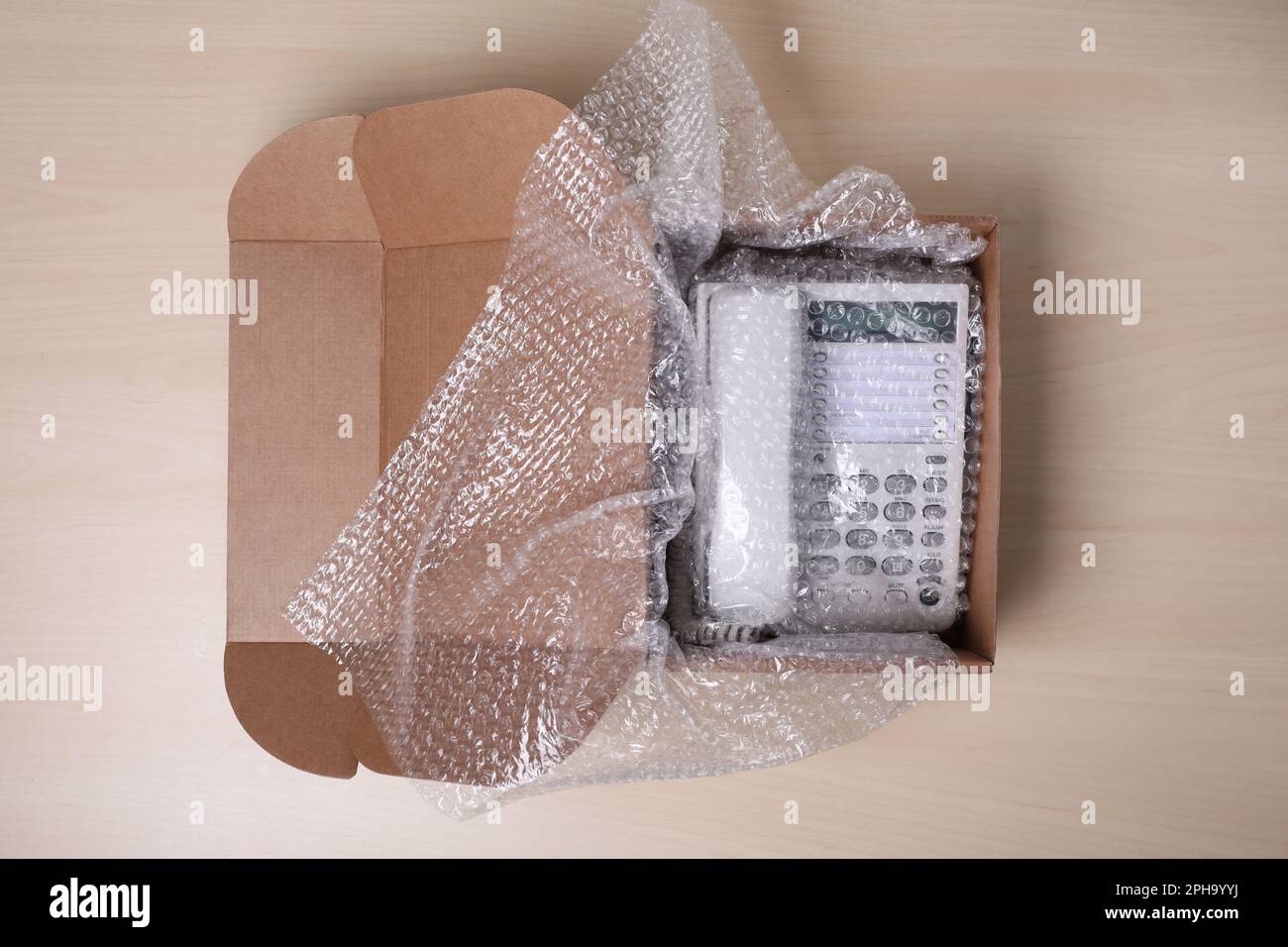 Corded phone with bubble wrap in cardboard box on wooden table, top ...