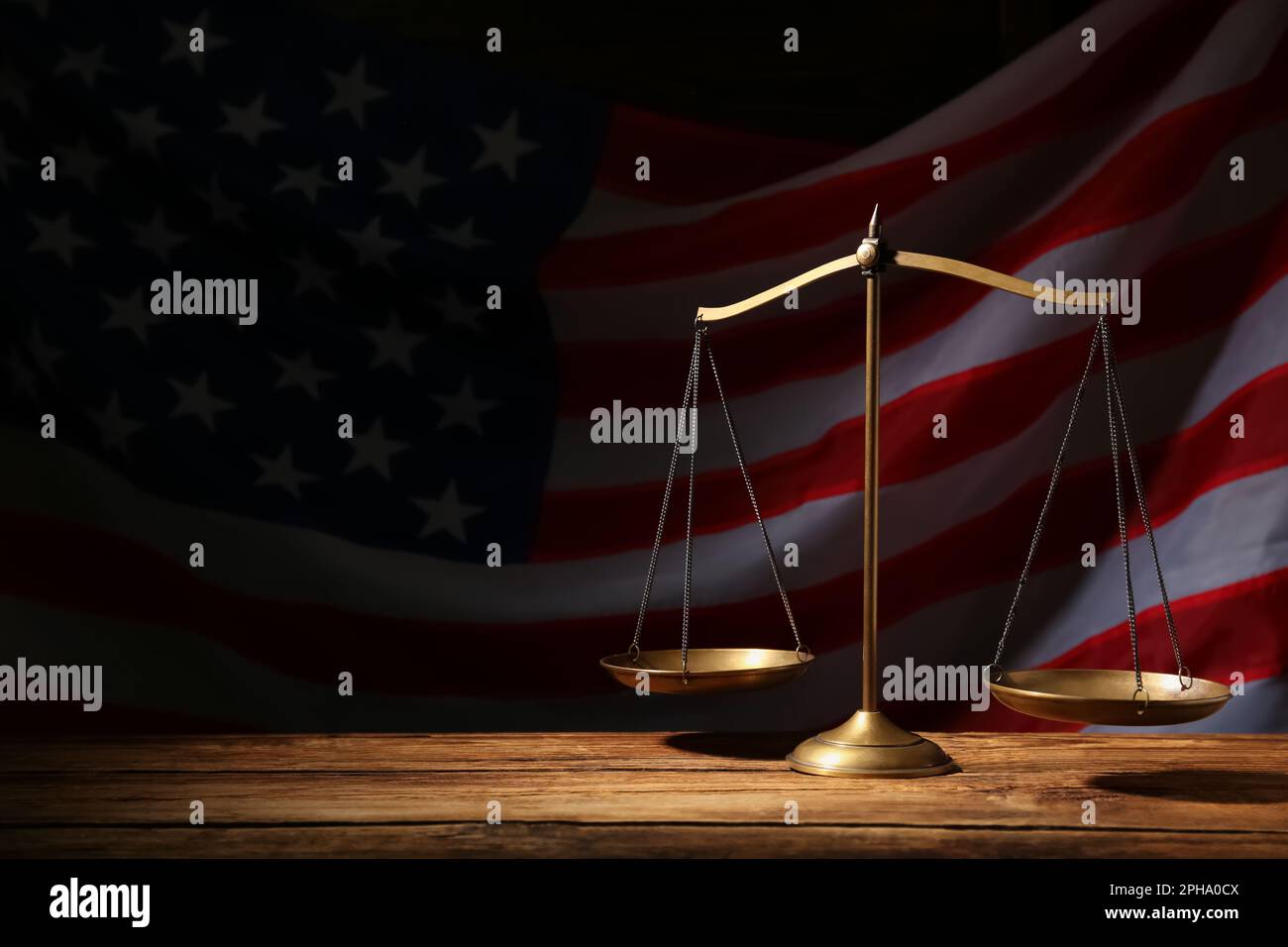 Scales of justice on wooden table against American flag in darkness ...