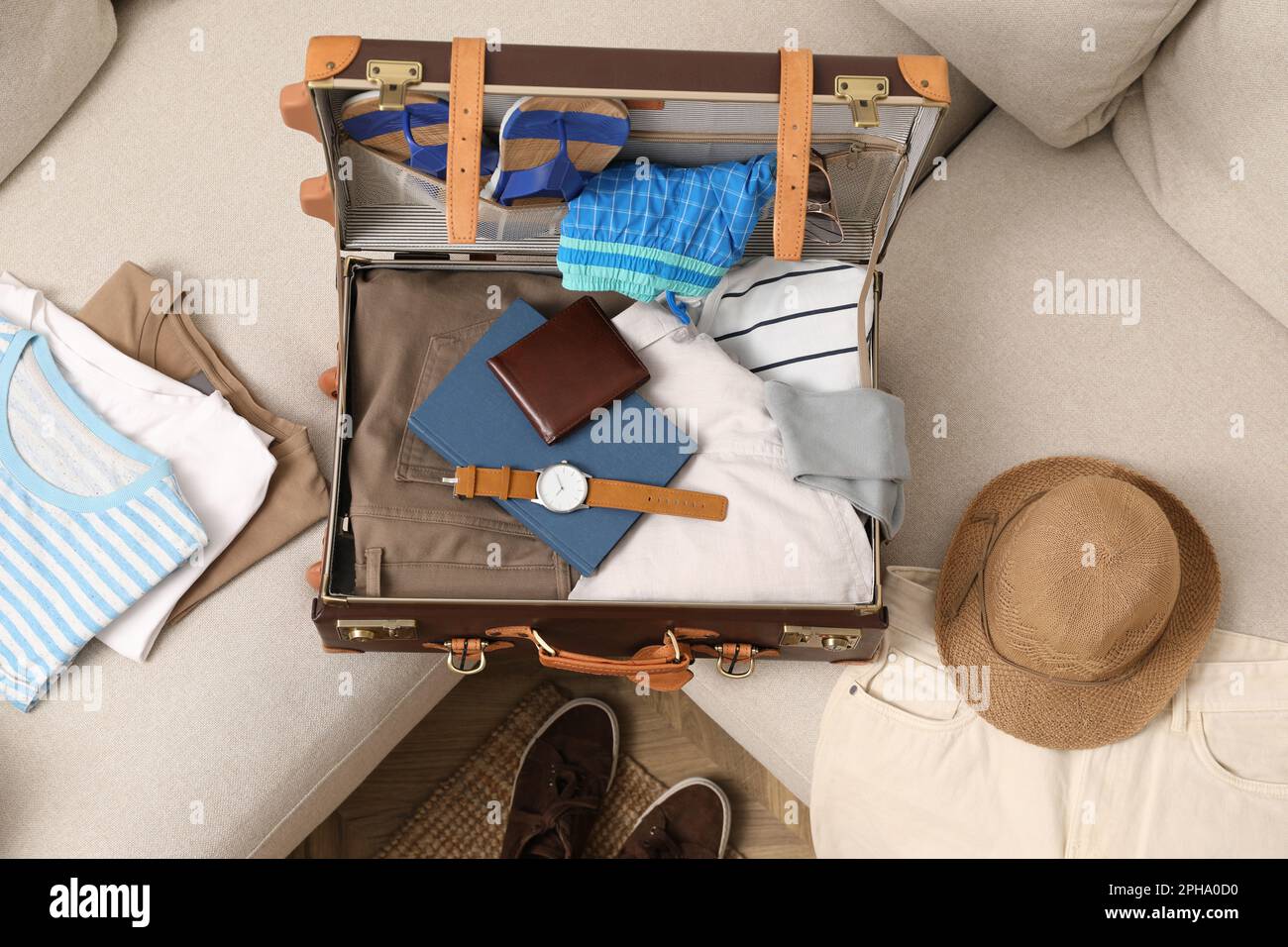 Open suitcase with different men clothes and accessories on sofa, top ...