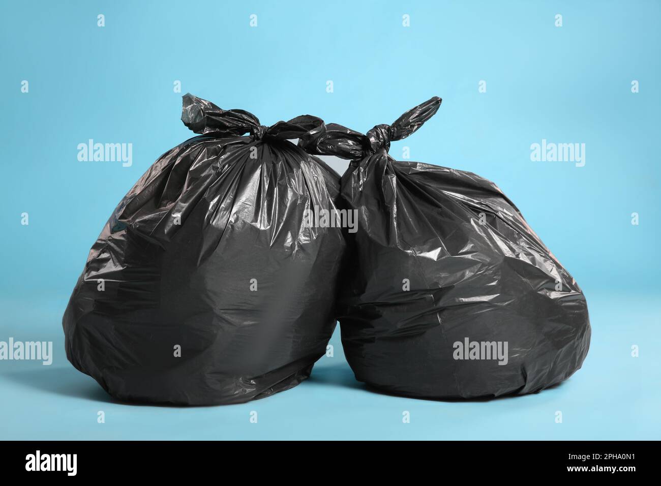 Black trash bags full of garbage on light blue background Stock Photo ...