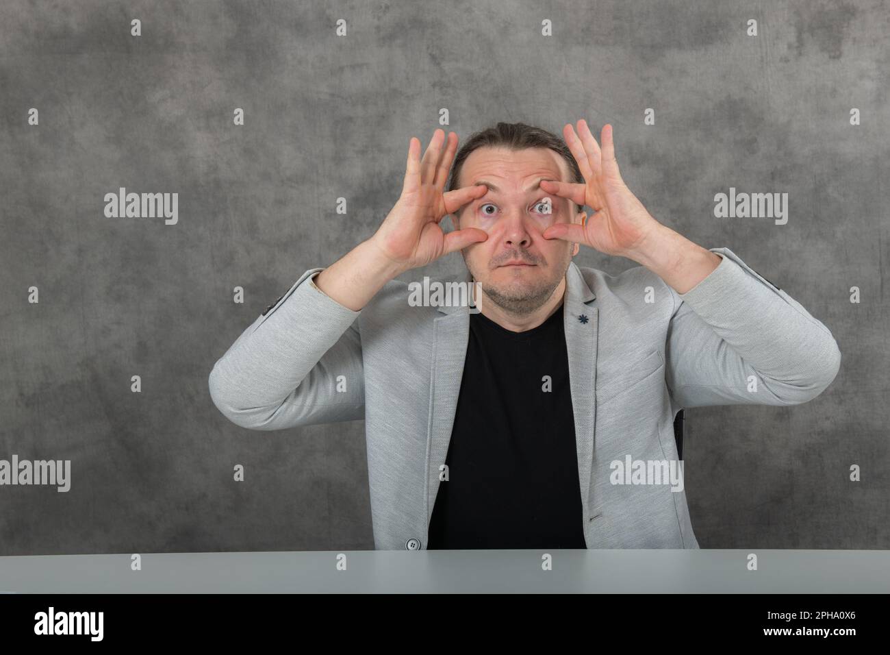 Looks ahead expanding his eyes with his fingers alone man in a gray ...