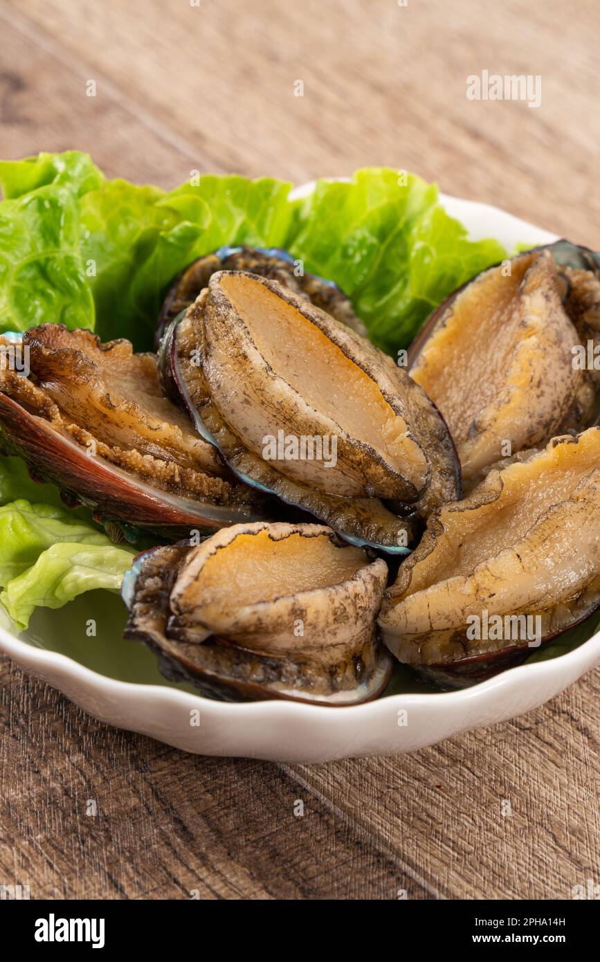 Delicious raw abalone in a plate with lettuce on wooden table ...