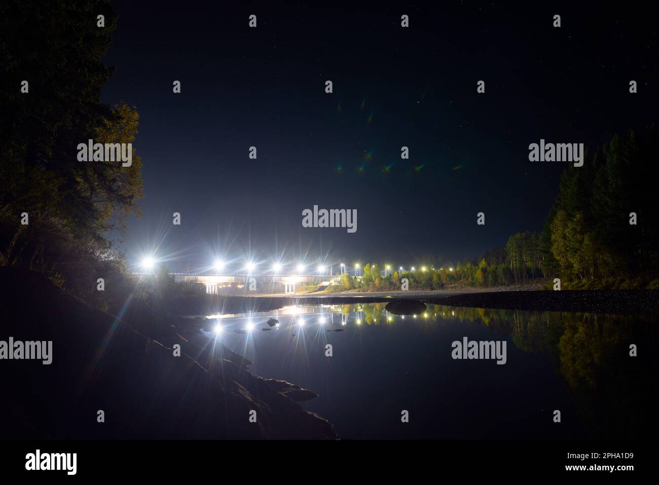 Bright light from the lanterns of the bridge on the river bank at night ...