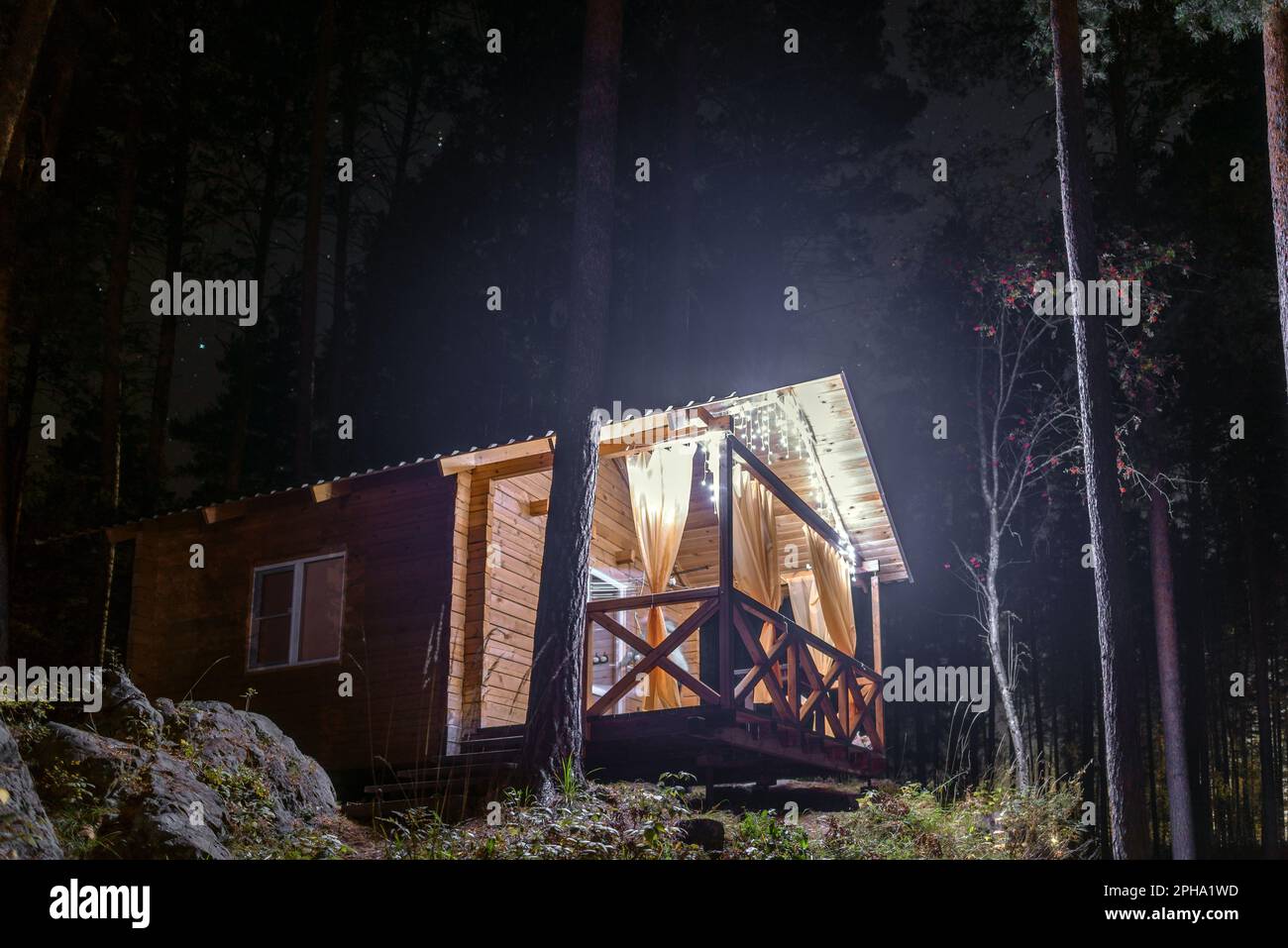 A wooden holiday cottage at night glows in the dark on a mountain in a ...